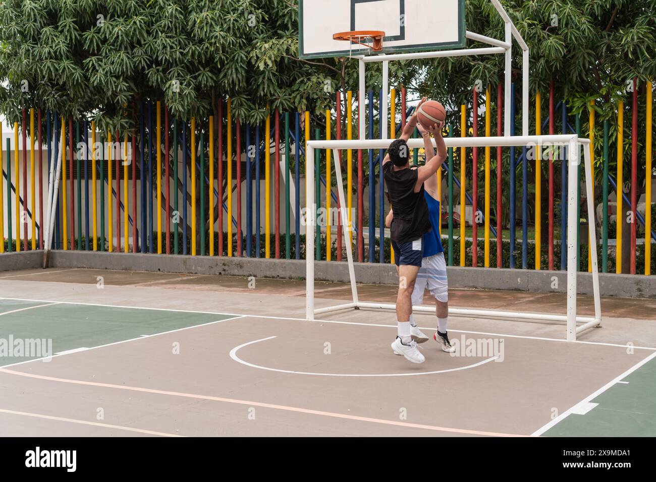 Two men playing basketball on an outdoor court, one jumping to block a ...