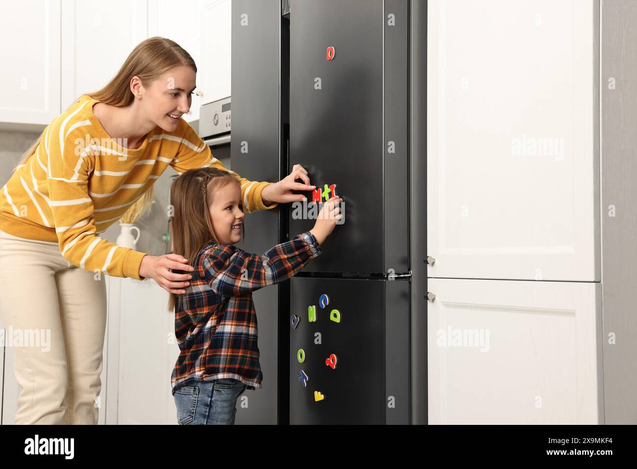 Mom and daughter putting magnetic letters on fridge at home. Learning ...