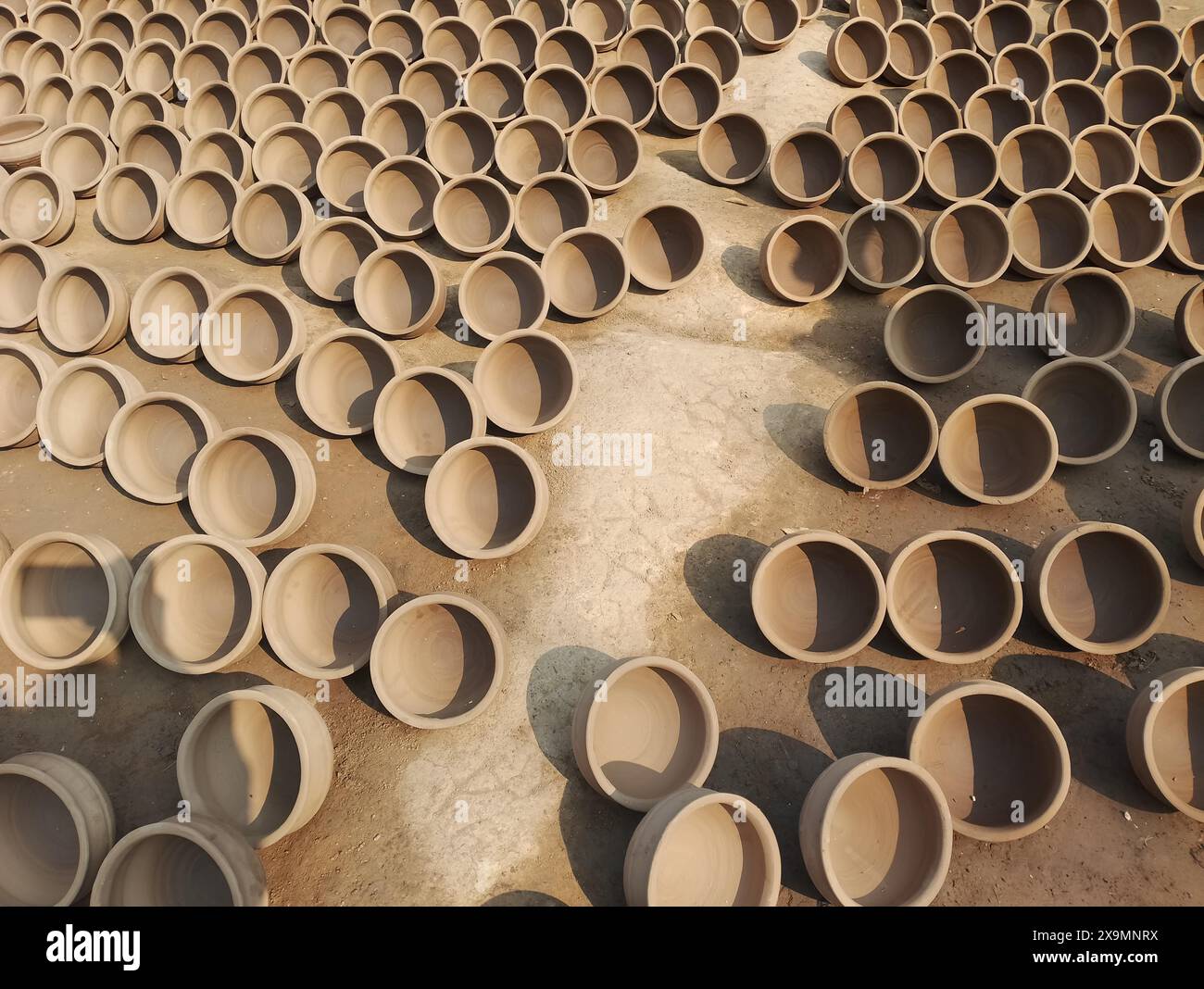 Rows of sunlit clay pots drying on the ground in an organized manner ...