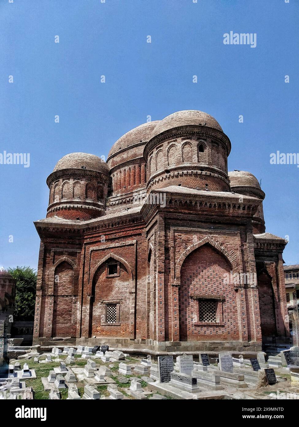 A brick mausoleum with multiple domes and arches under a clear sky ...