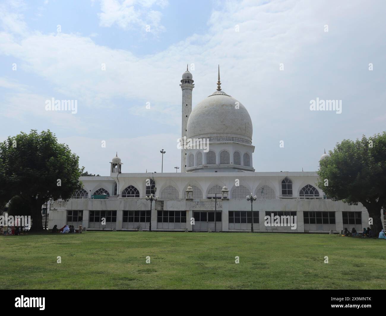 A white mosque with a large dome and minaret, surrounded by trees and ...