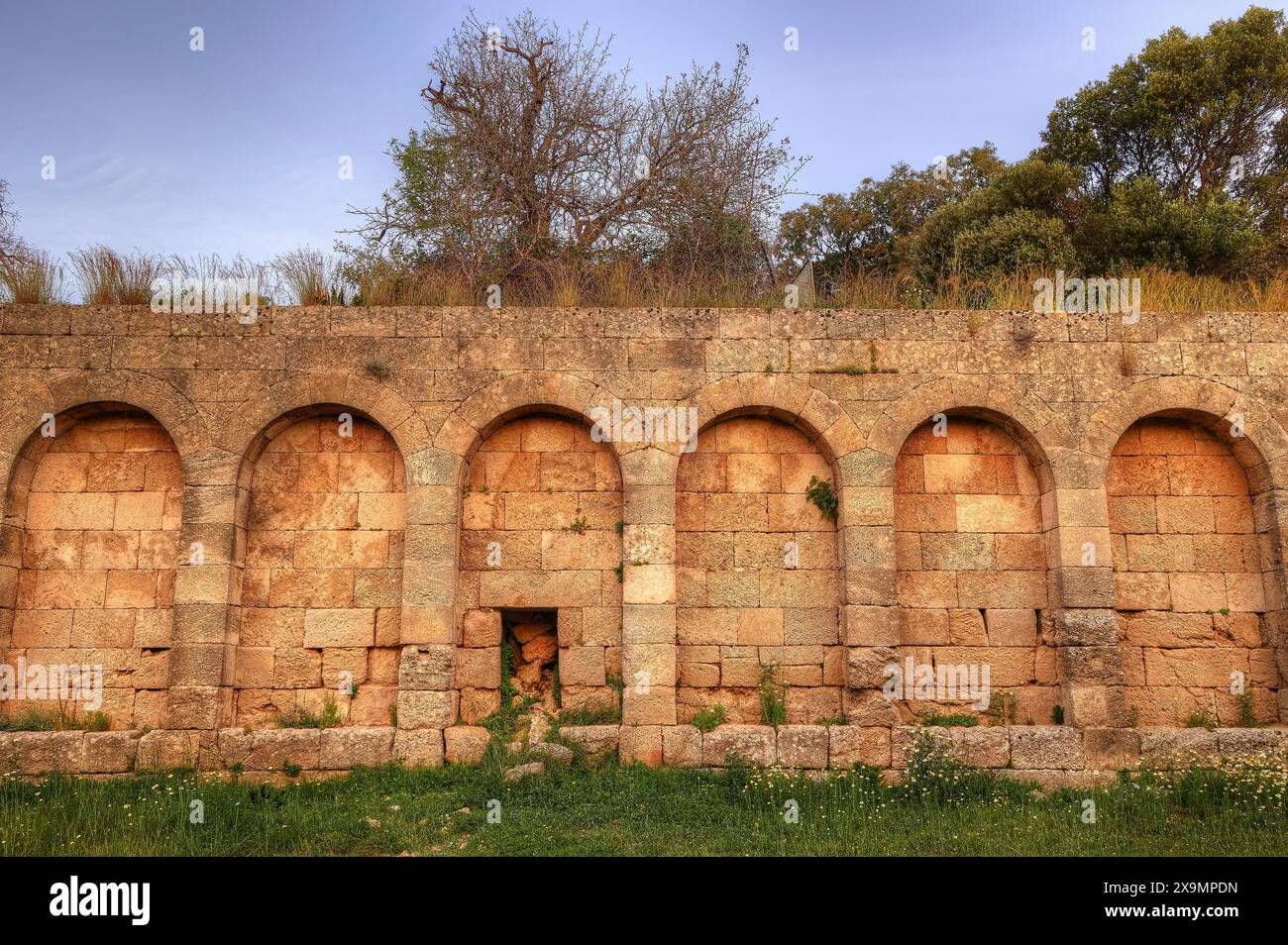 Next to amphitheatre, Ancient stone wall with several arches surrounded ...