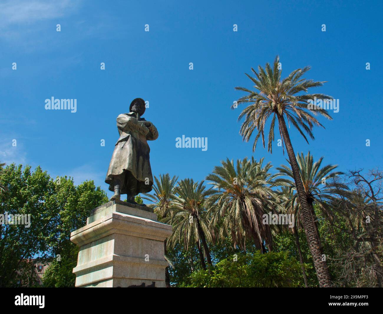 A statue raised against a blue sky and surrounded by palm trees ...