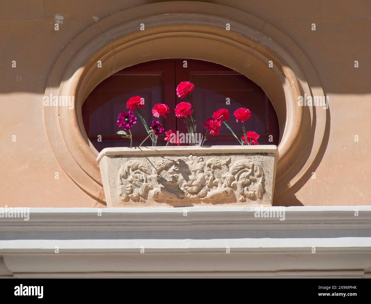 An oval window with a decorative flower box full of red flowers in ...