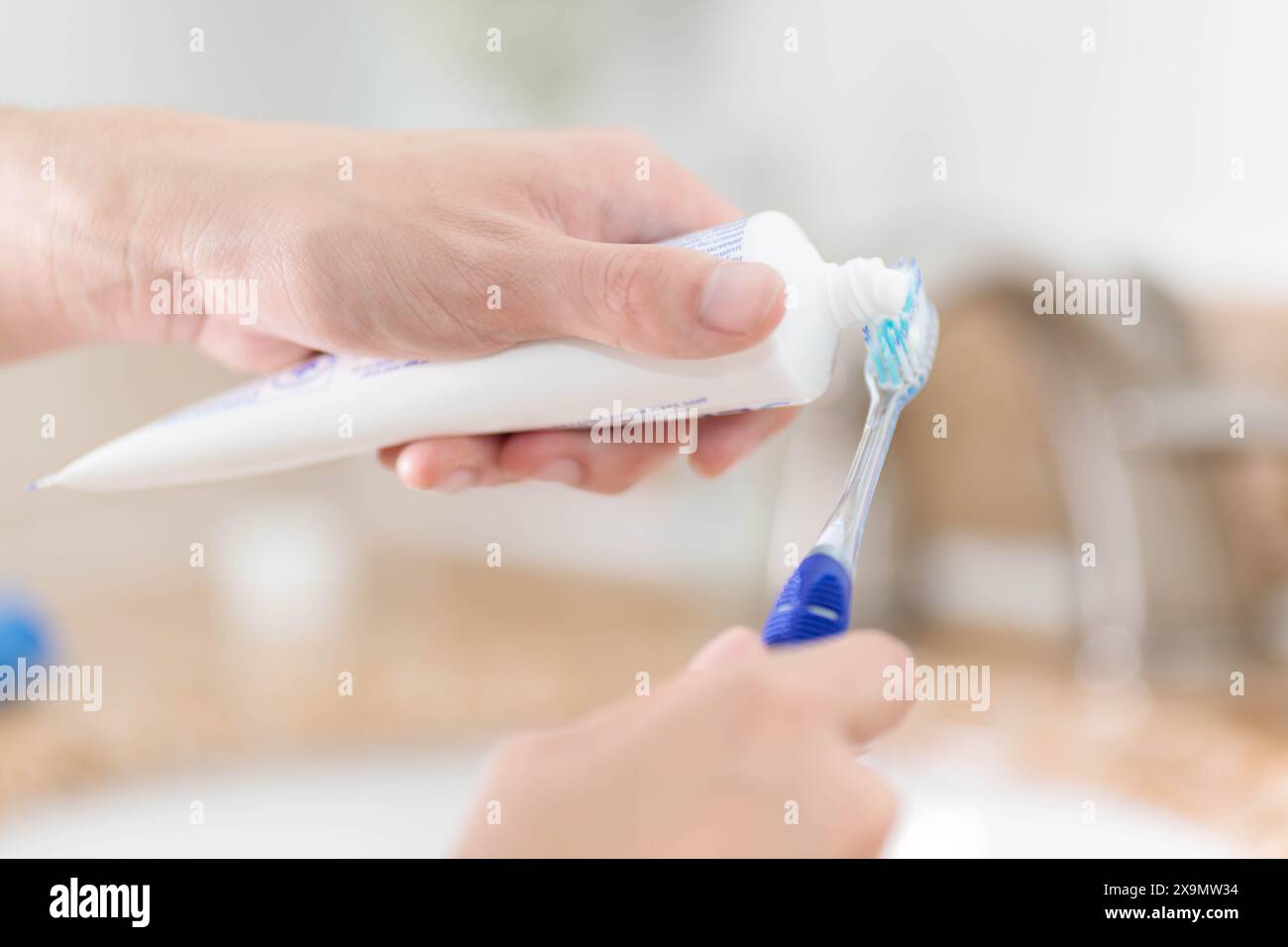 Some hands are squirting toothpaste onto a toothbrush over the bathroom ...