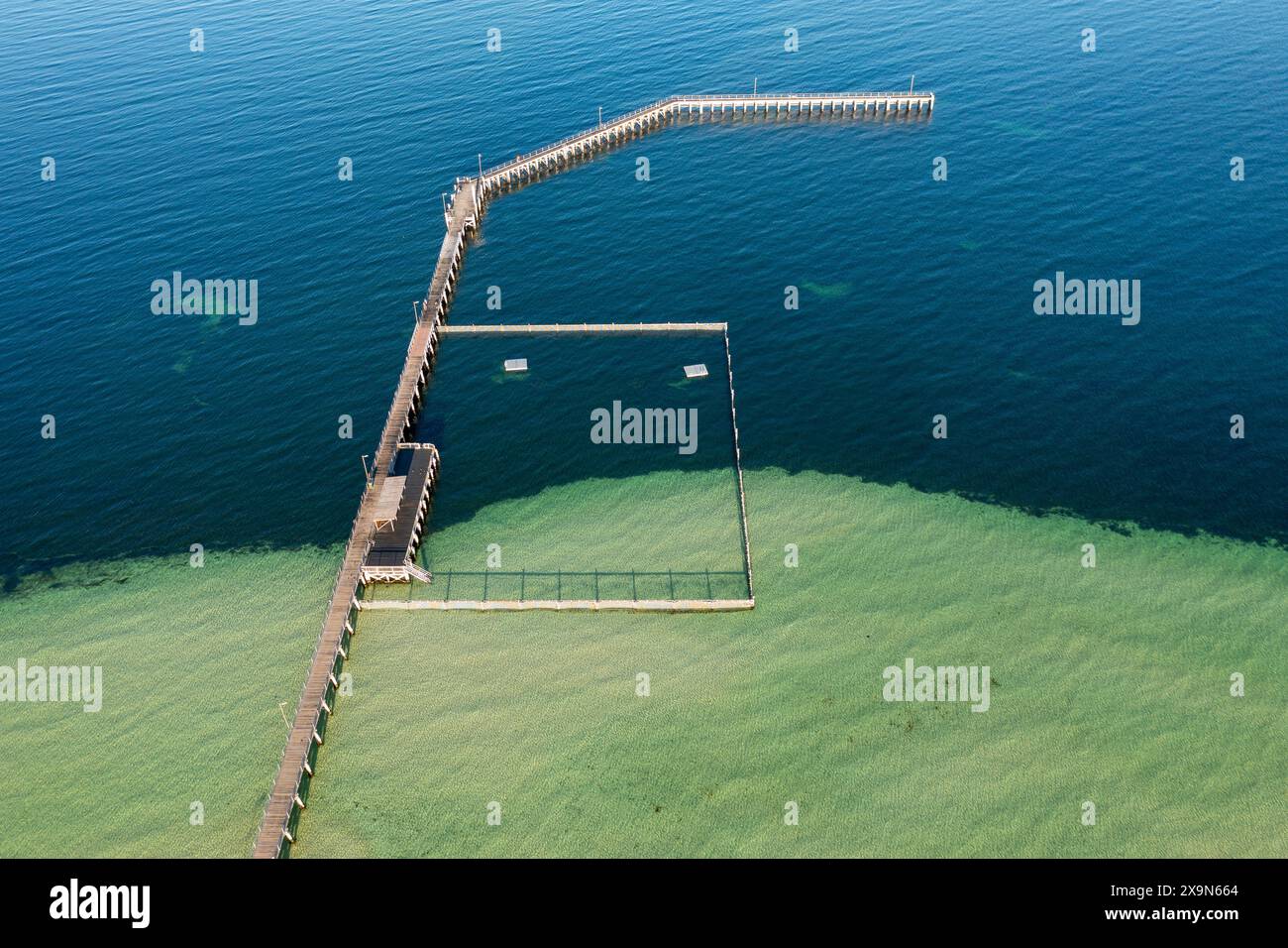 Aerial view of a swimming pen on the the side of a long curved jetty ...