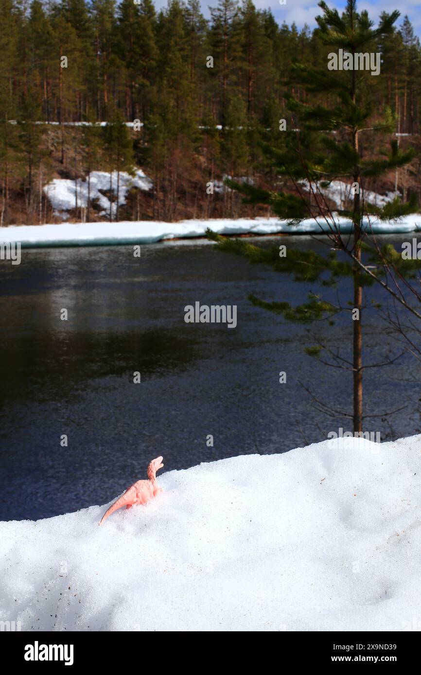 Toy dinosaur standing in the melting snow at riverside in northern ...