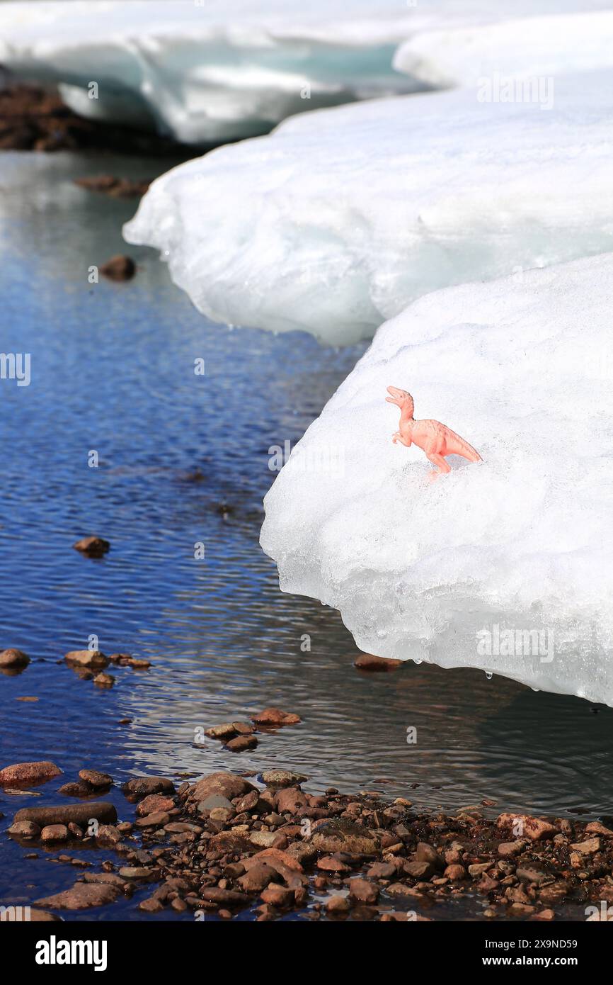 Toy dinosaur standing on melting ice at riverside in northern Sweden ...