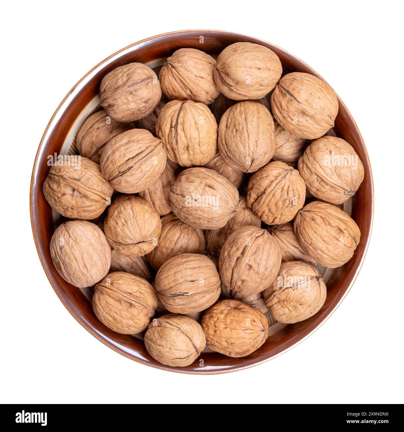 Walnuts in their shells, in a brown bowl. Unshelled dried seeds of the common walnut tree ...