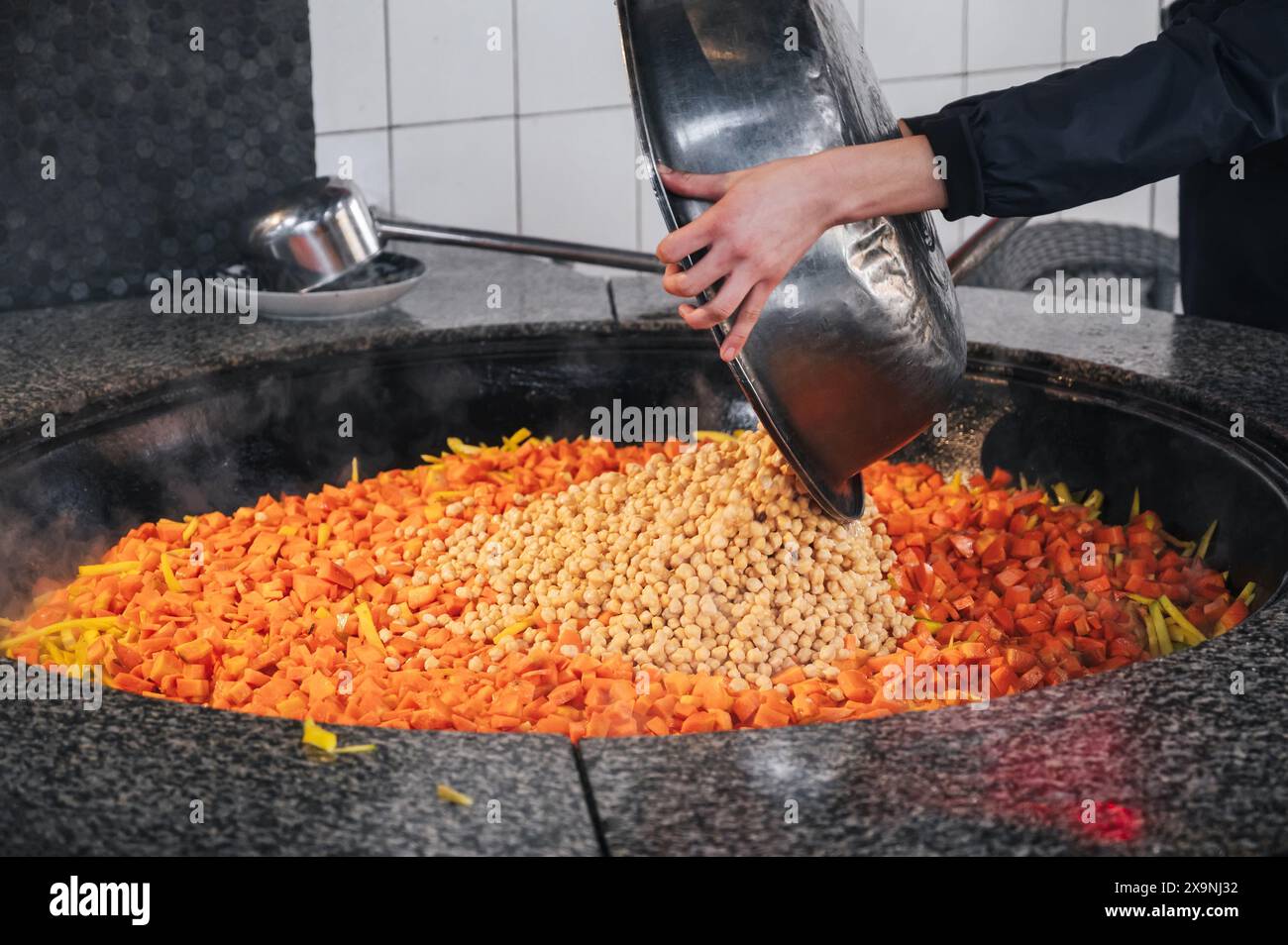 male chef adds chickpeas to cauldron with carrots to cook traditional ...