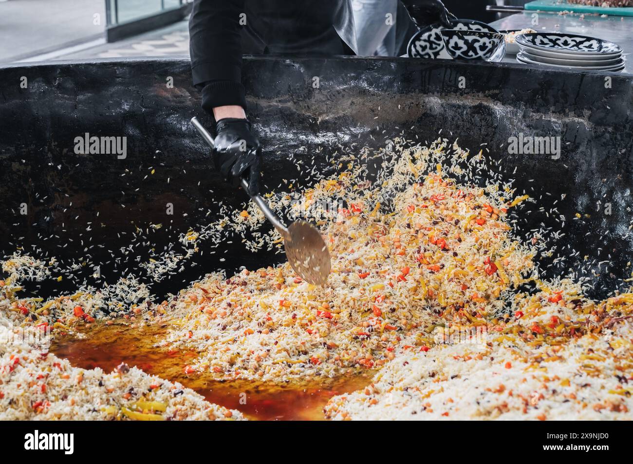 man cook puts cooked Uzbek pilaf from cauldron on plate. Traditional ...