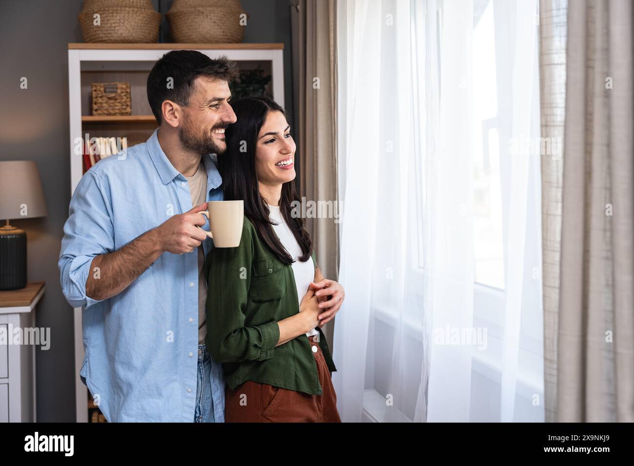 Young newlywed couple standing near window at their new apartment ...