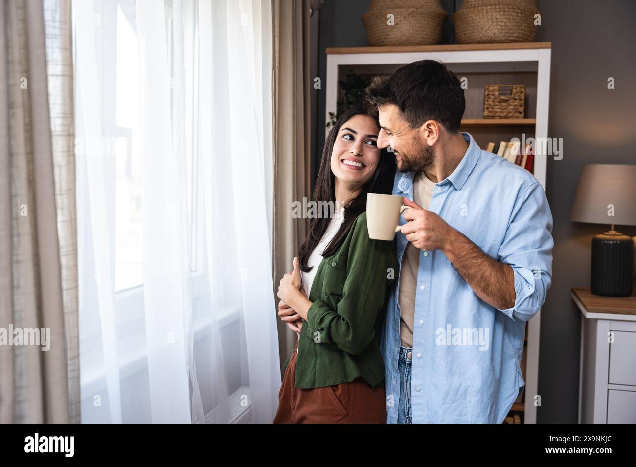 Young newlywed couple standing near window at their new apartment ...