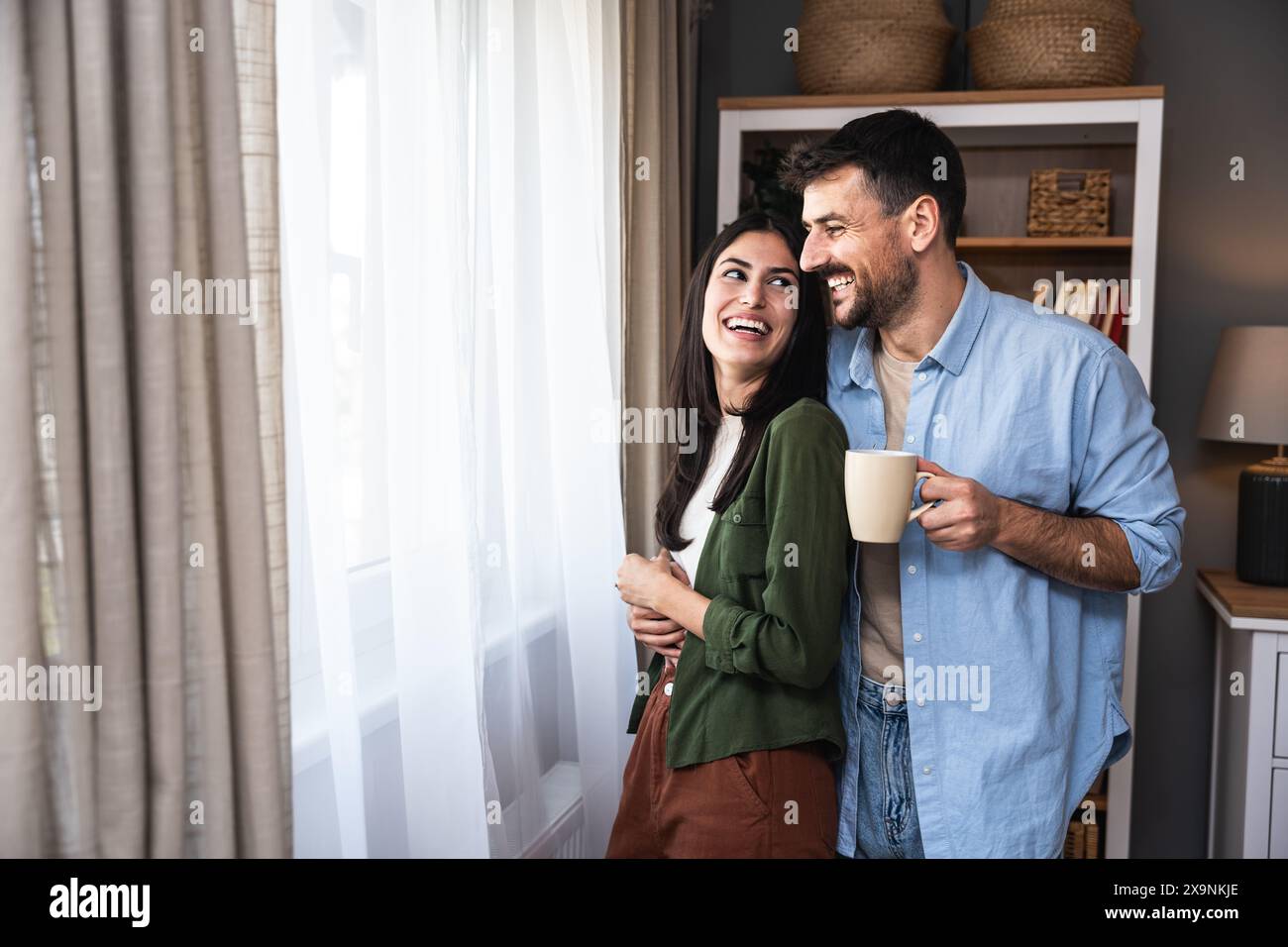 Young newlywed couple standing near window at their new apartment ...