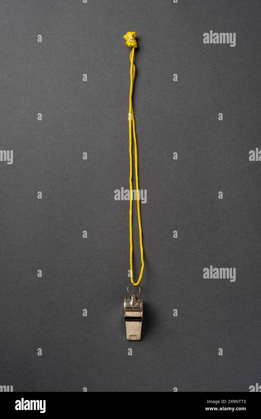 Top view of metal whistle with yellow string on dark gray background ...