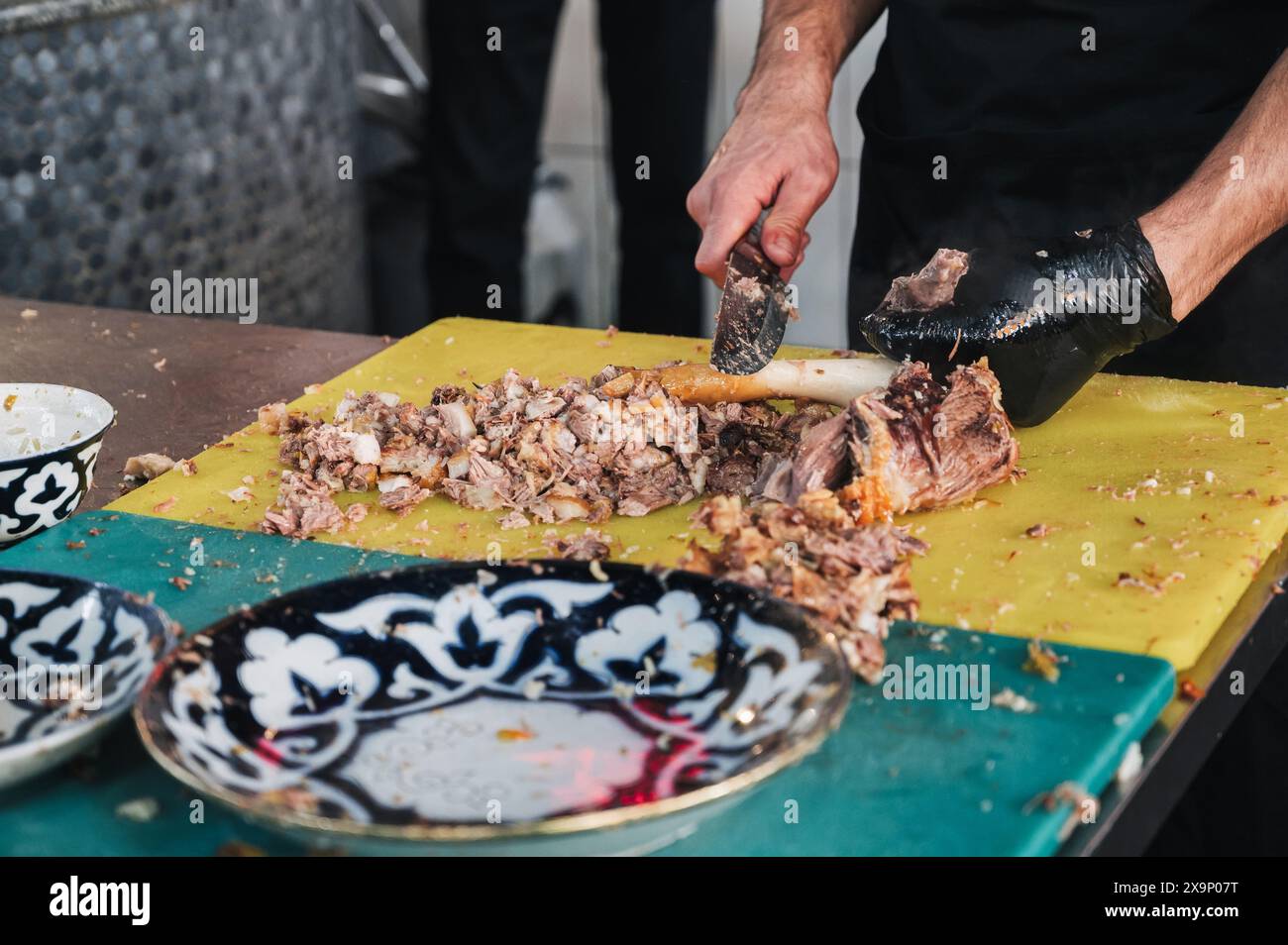 male chef cuts boiled meat from a lamb bone with a knife to cook ...