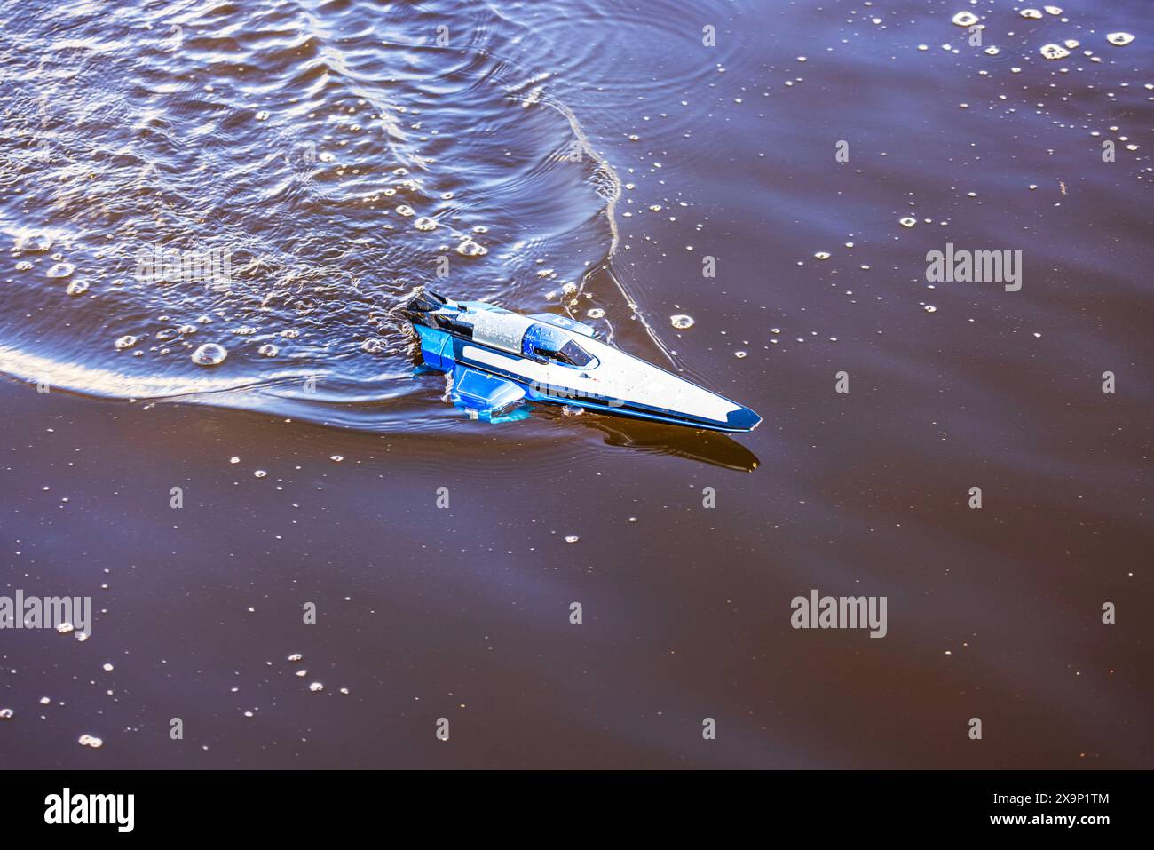 Close-up view of a remote-controlled blue and white speedboat creating ...