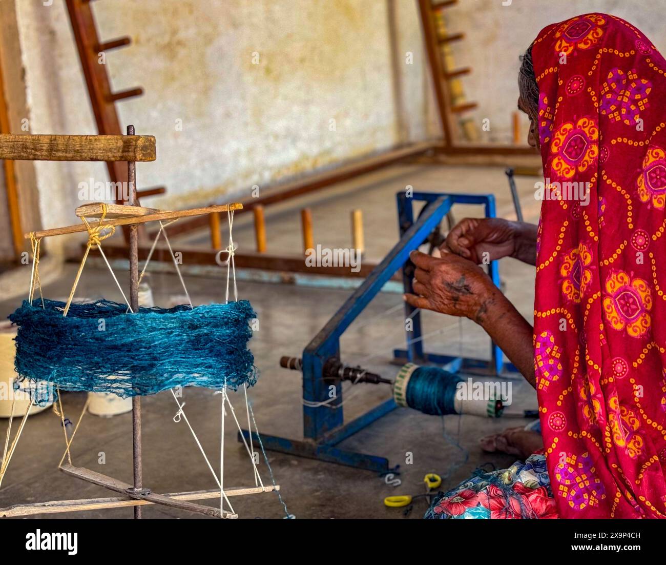 Skilled weaver in a vibrant saree manually operates a spinning wheel ...