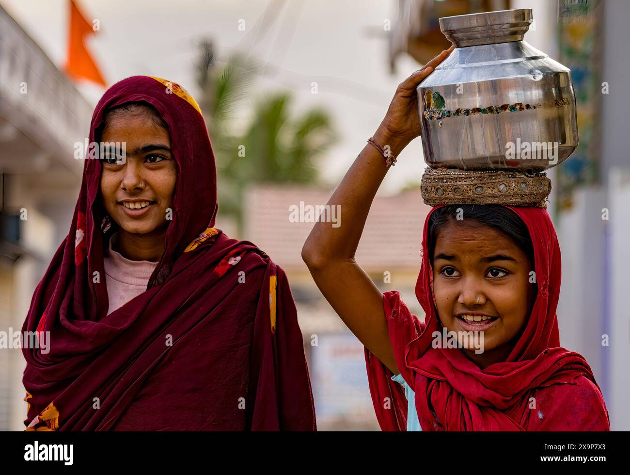 Two young women in vibrant attire balancing water pots on heads with ...