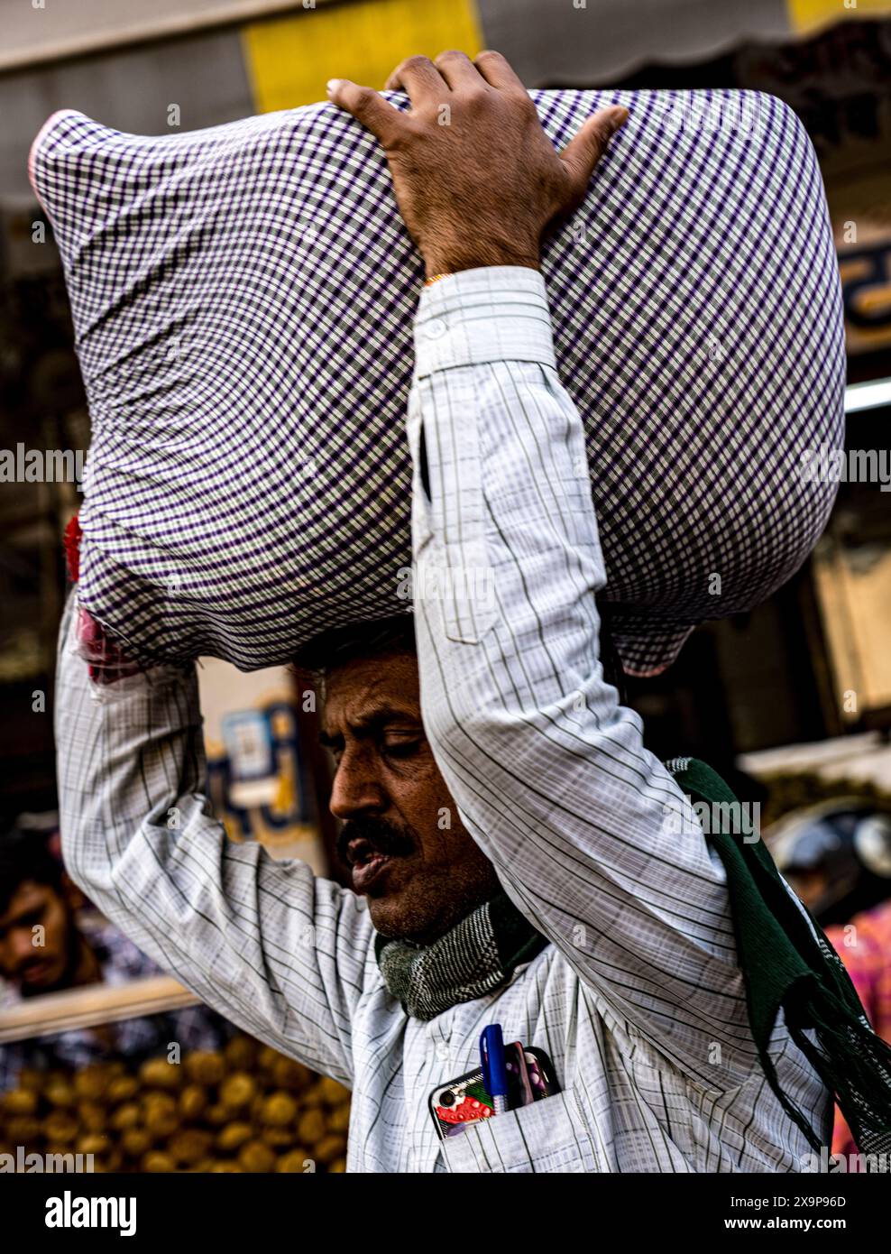 Man strains to carry a large sack on his head through a bustling market ...
