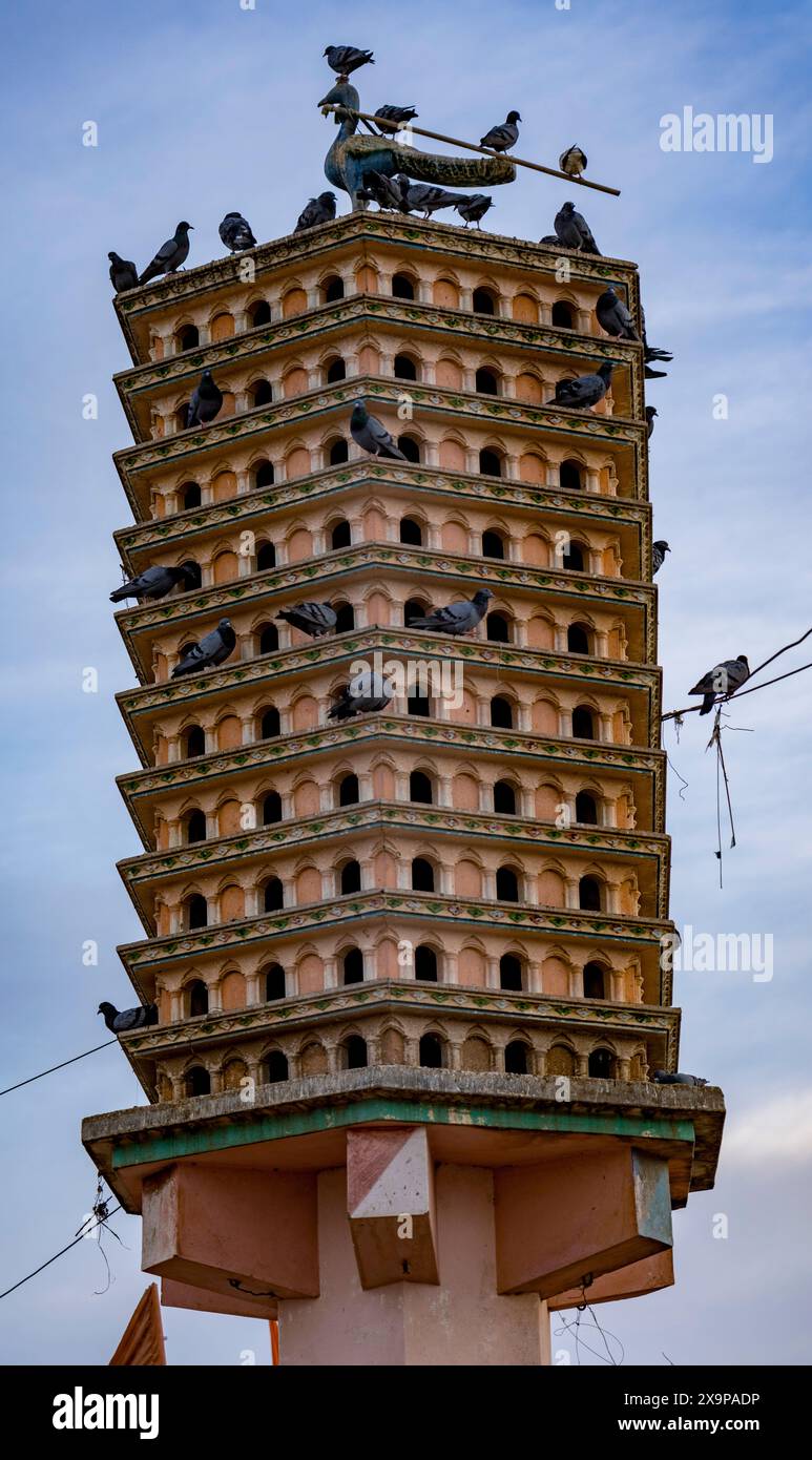 Tall pigeon tower filled with birds, standing stark against a cloudy ...