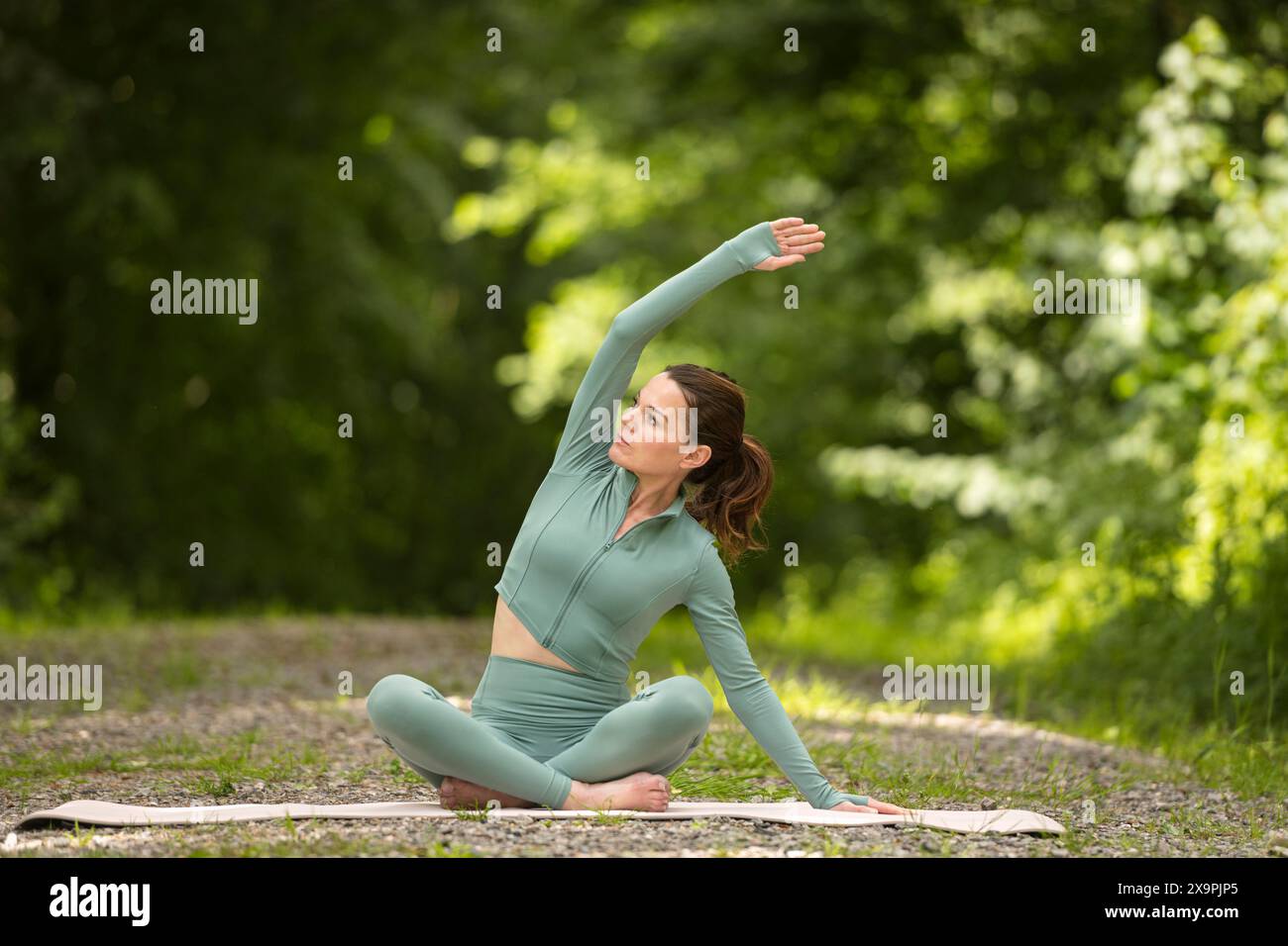 Fit, sporty woman doing arm stretching exercises sitting outside on a ...