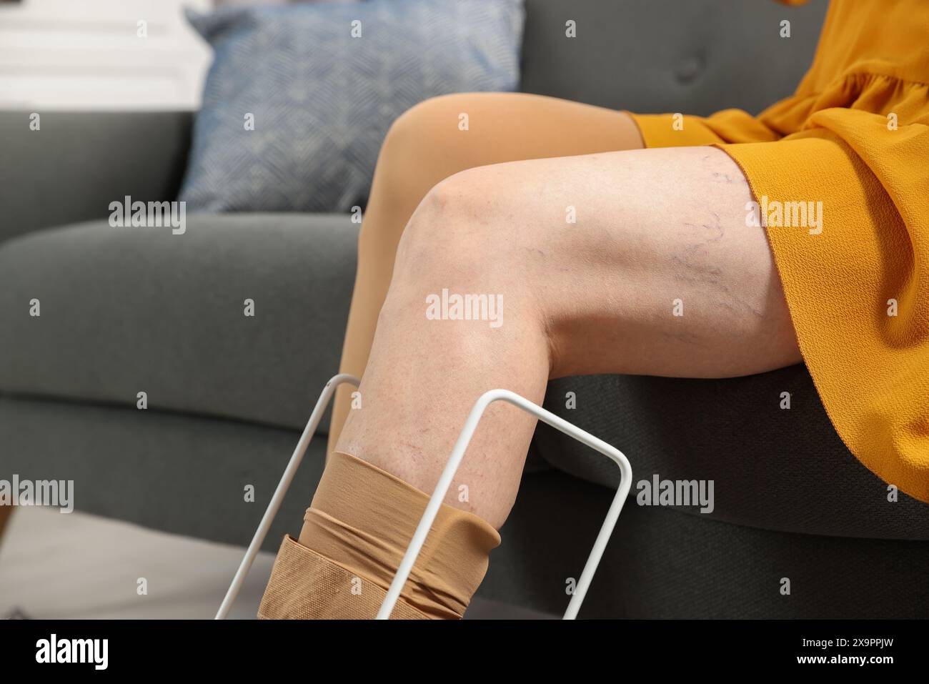 Woman putting on compression tights with stocking donner in living room ...