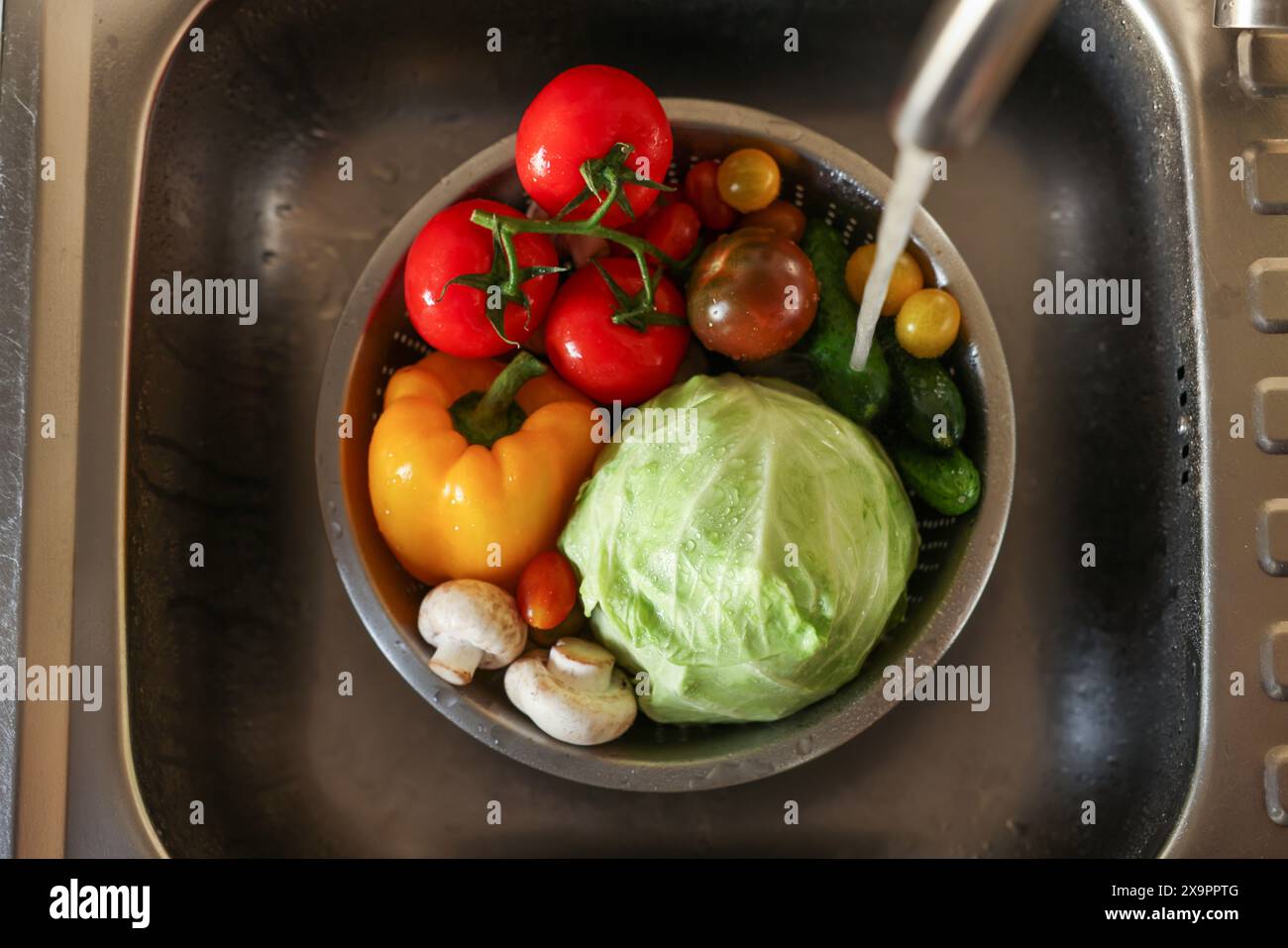 Washing different vegetables with tap water in metal colander inside ...