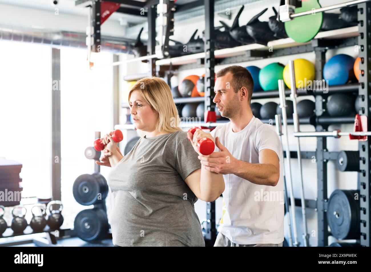 Overweight woman exercising in gym, using dumbbells. Personal trainer ...