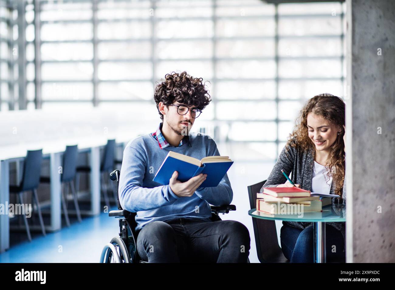 Handsome university student in wheelchair studying in library with ...