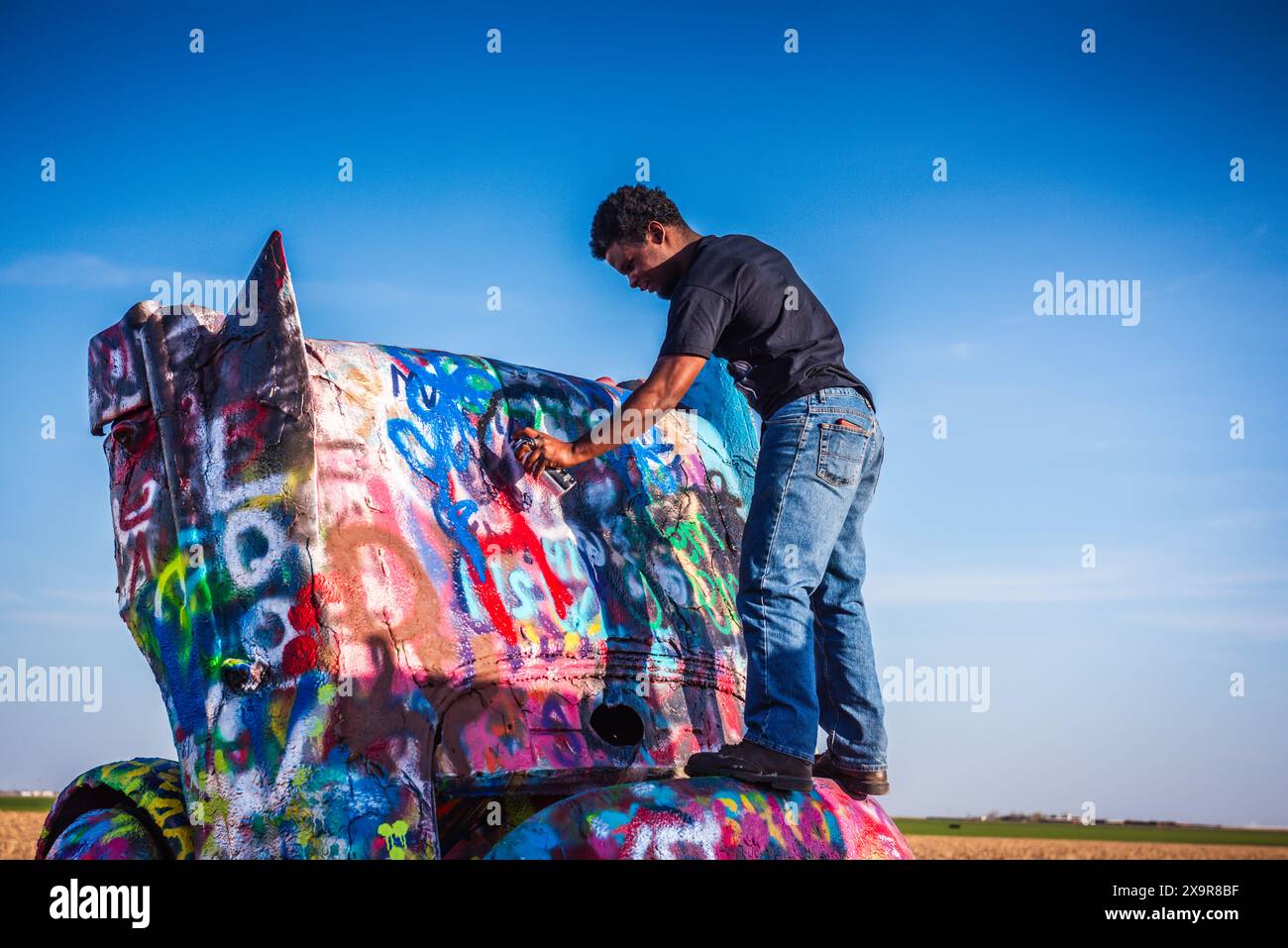 Young man spray painting car at Cadillac Ranch, the public art ...