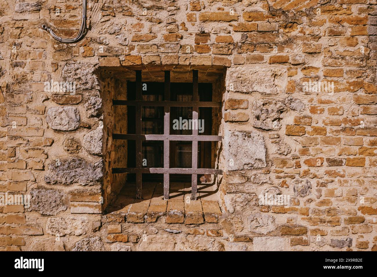 An old square window built into a rustic brick wall with metal bars ...
