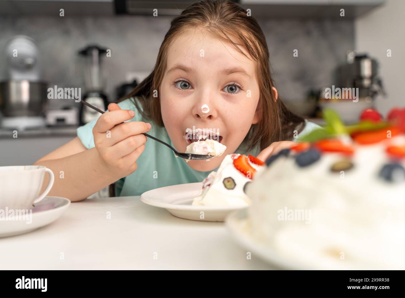 Little girl eating cake while sitting in the kitchen. A pre-teenage ...