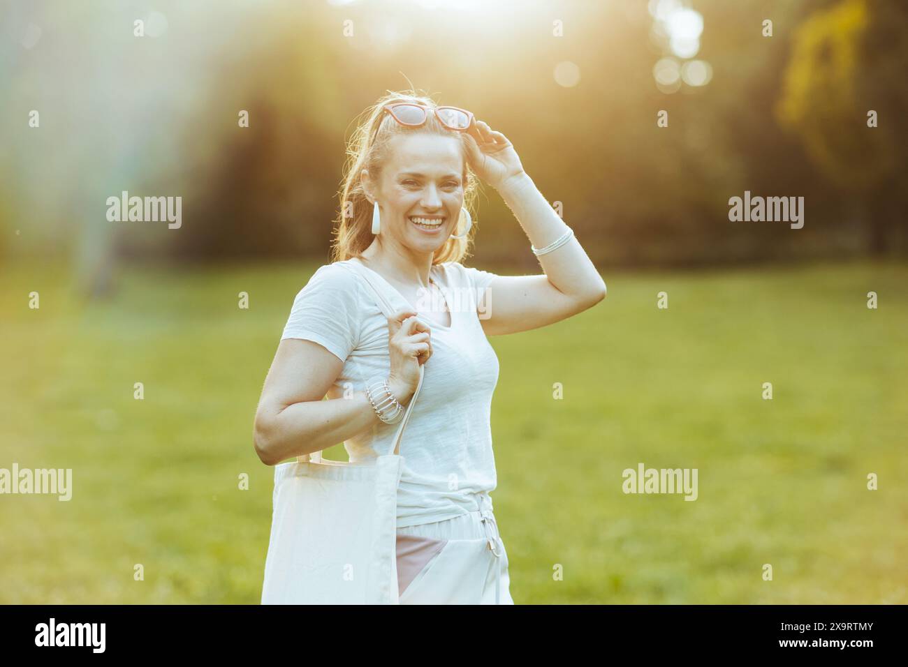 Summer time. happy trendy 40 years old woman in white shirt with tote ...