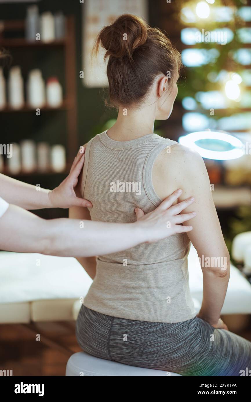 Healthcare time. Seen from behind medical massage therapist in spa salon checking clients back ...
