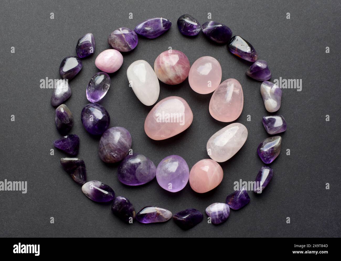 Natural rose quartz and amethyst crystals are laid out in a spiral ...
