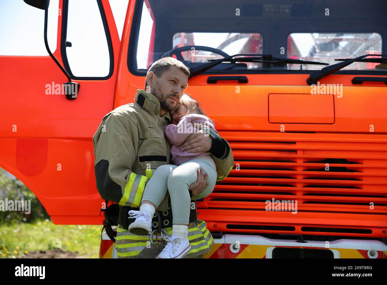 Firefighter in uniform holding rescued little girl near fire truck ...