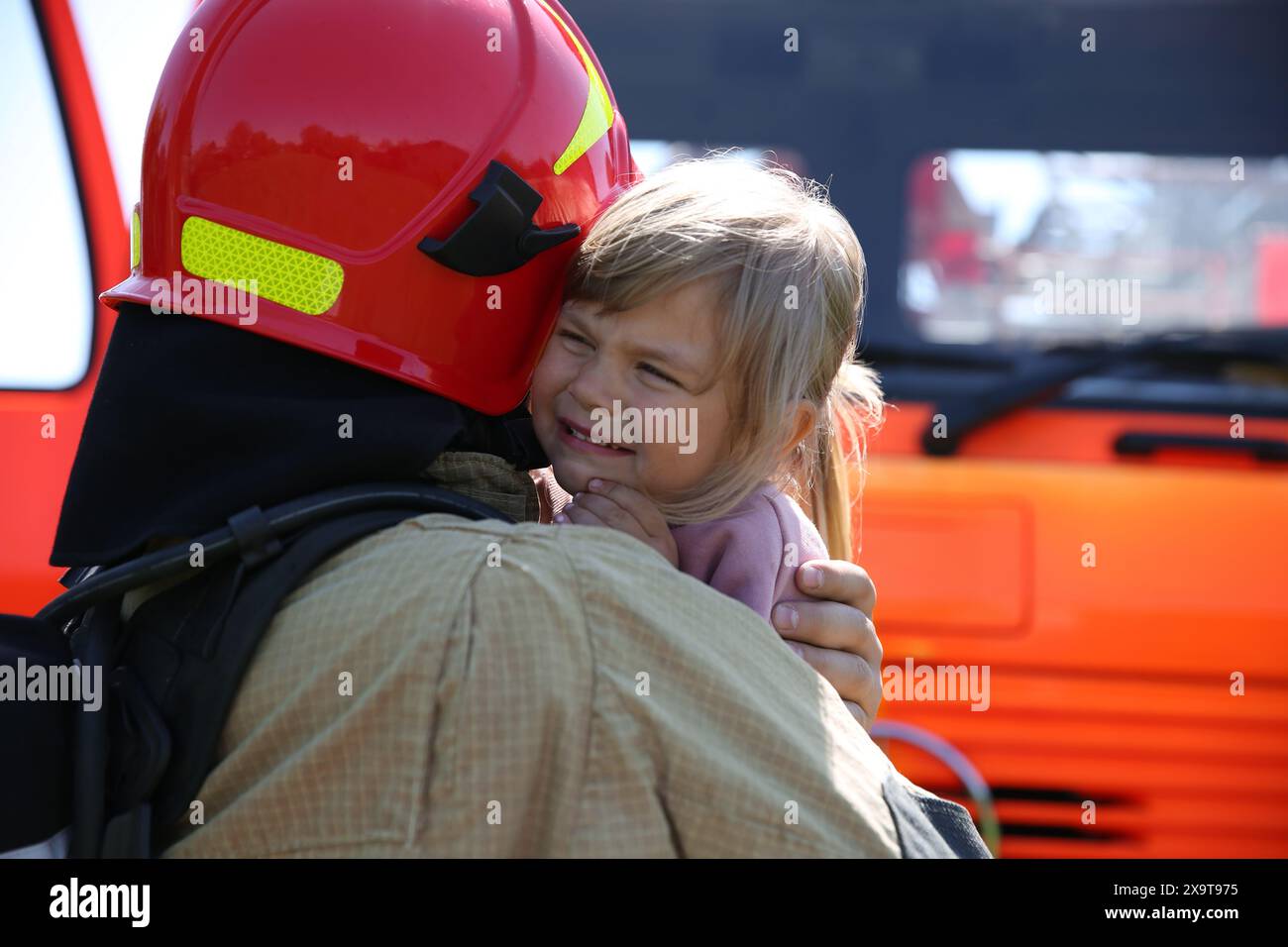 Firefighter in uniform holding rescued little girl near fire truck ...