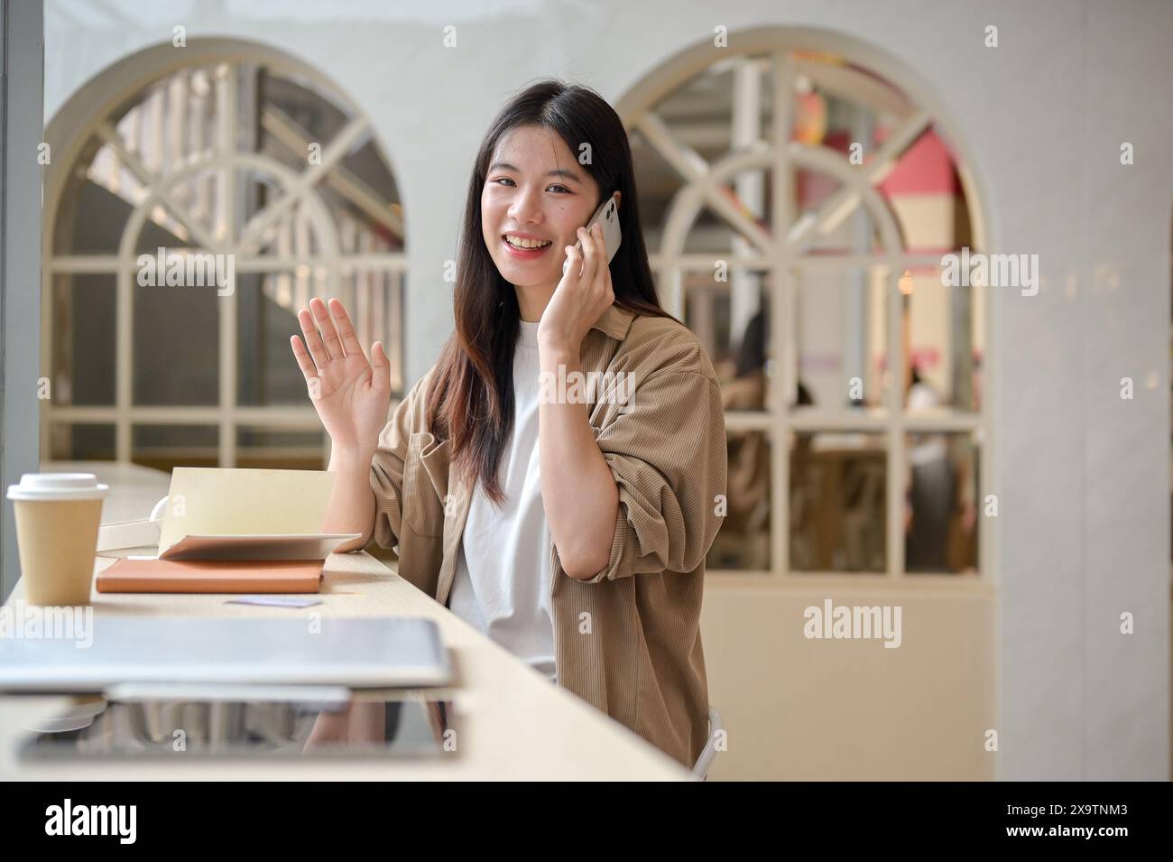 An attractive young Asian woman is waving her hand to greet someone ...