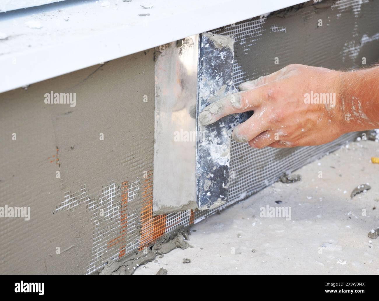 The builder applies plaster with a spatula to the reinforcing mesh on top of a layer of rigid ...