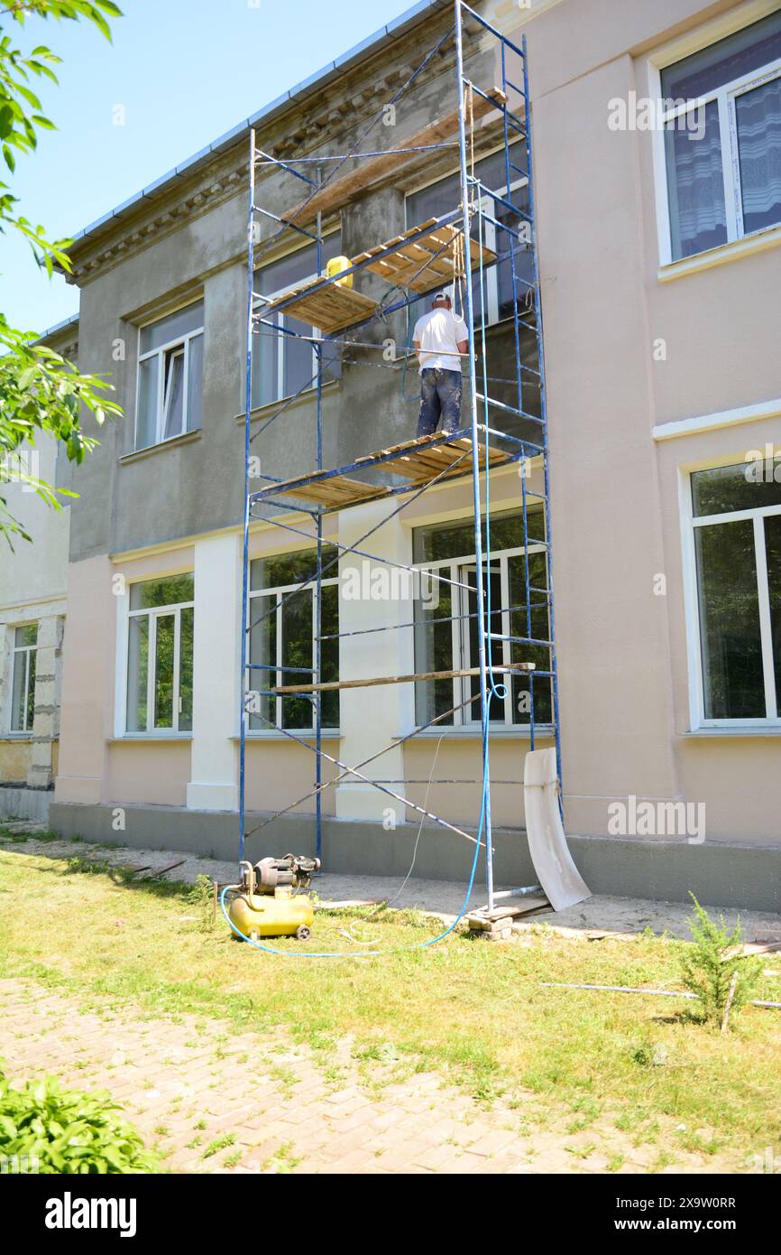 A builder repairs the facade of a house and applies new plaster before ...