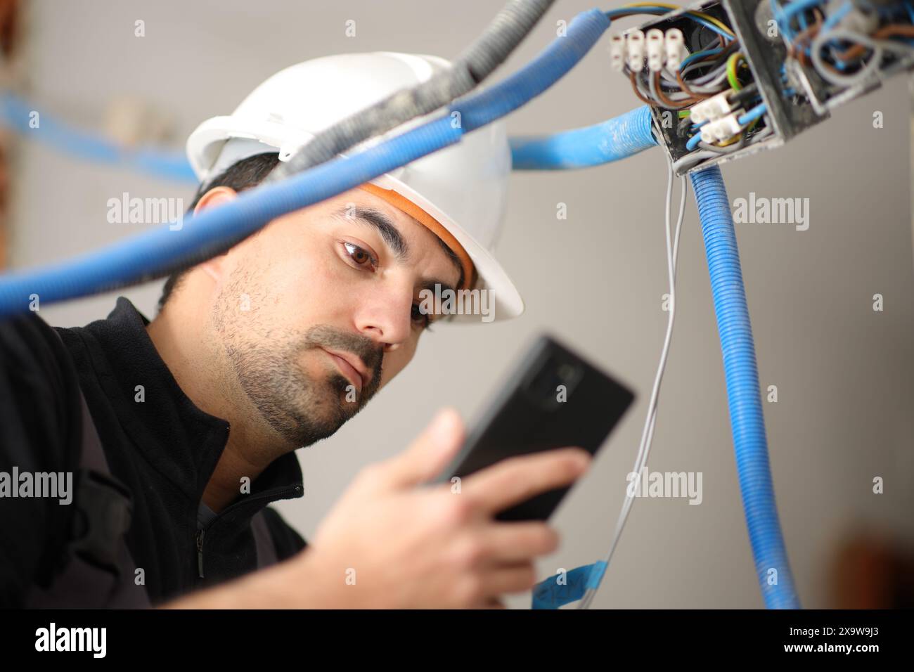 Electrician checking information on phone installing electrical system ...