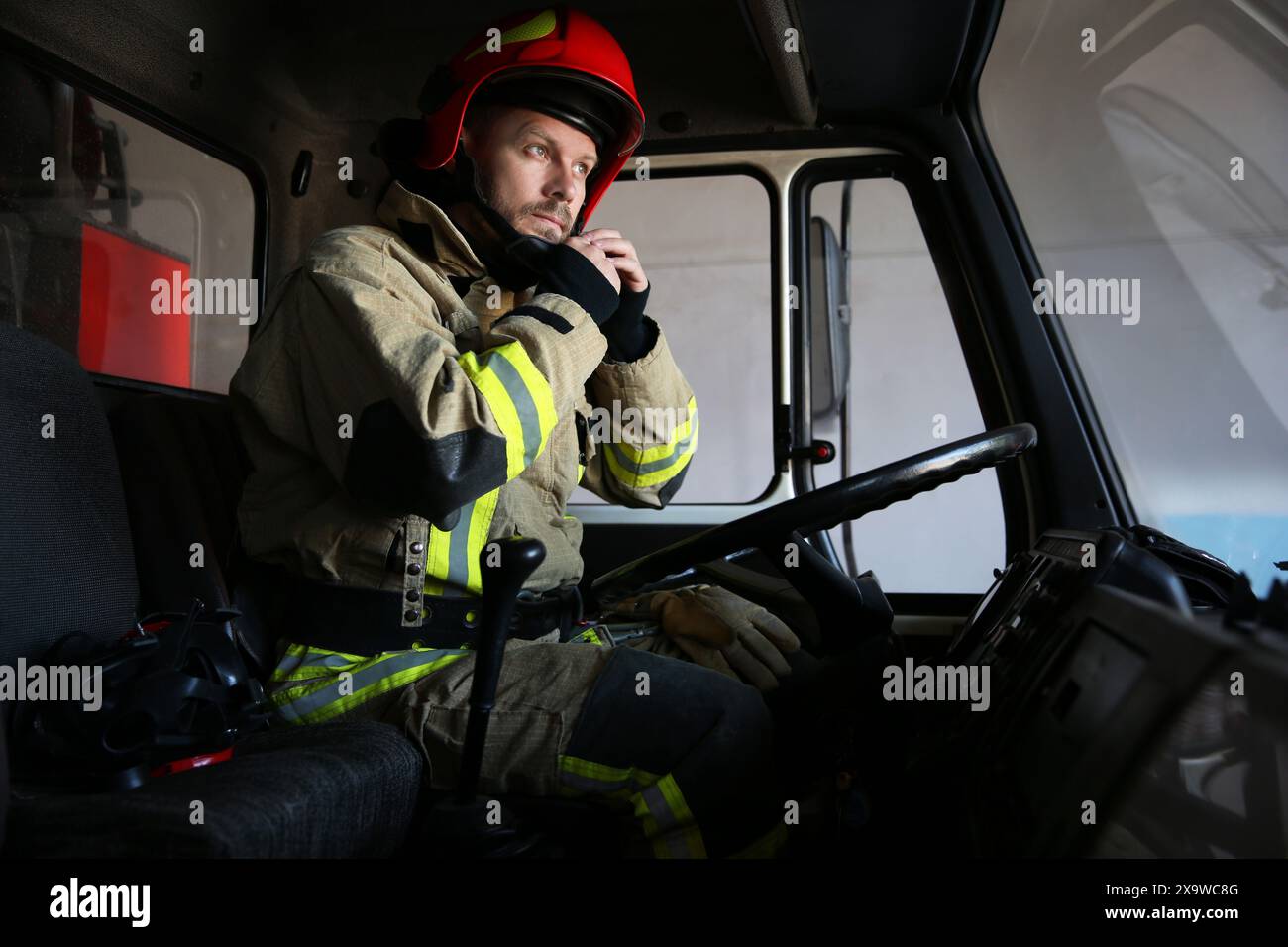 Firefighter in uniform wearing helmet inside fire truck Stock Photo - Alamy