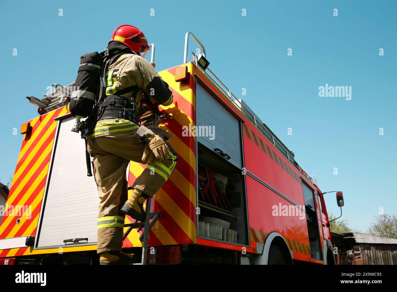 Firefighter in uniform on fire truck outdoors, back view Stock Photo ...