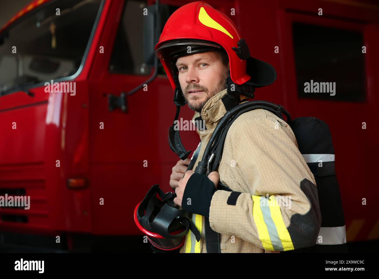 Portrait of firefighter in uniform near red fire truck at station Stock ...