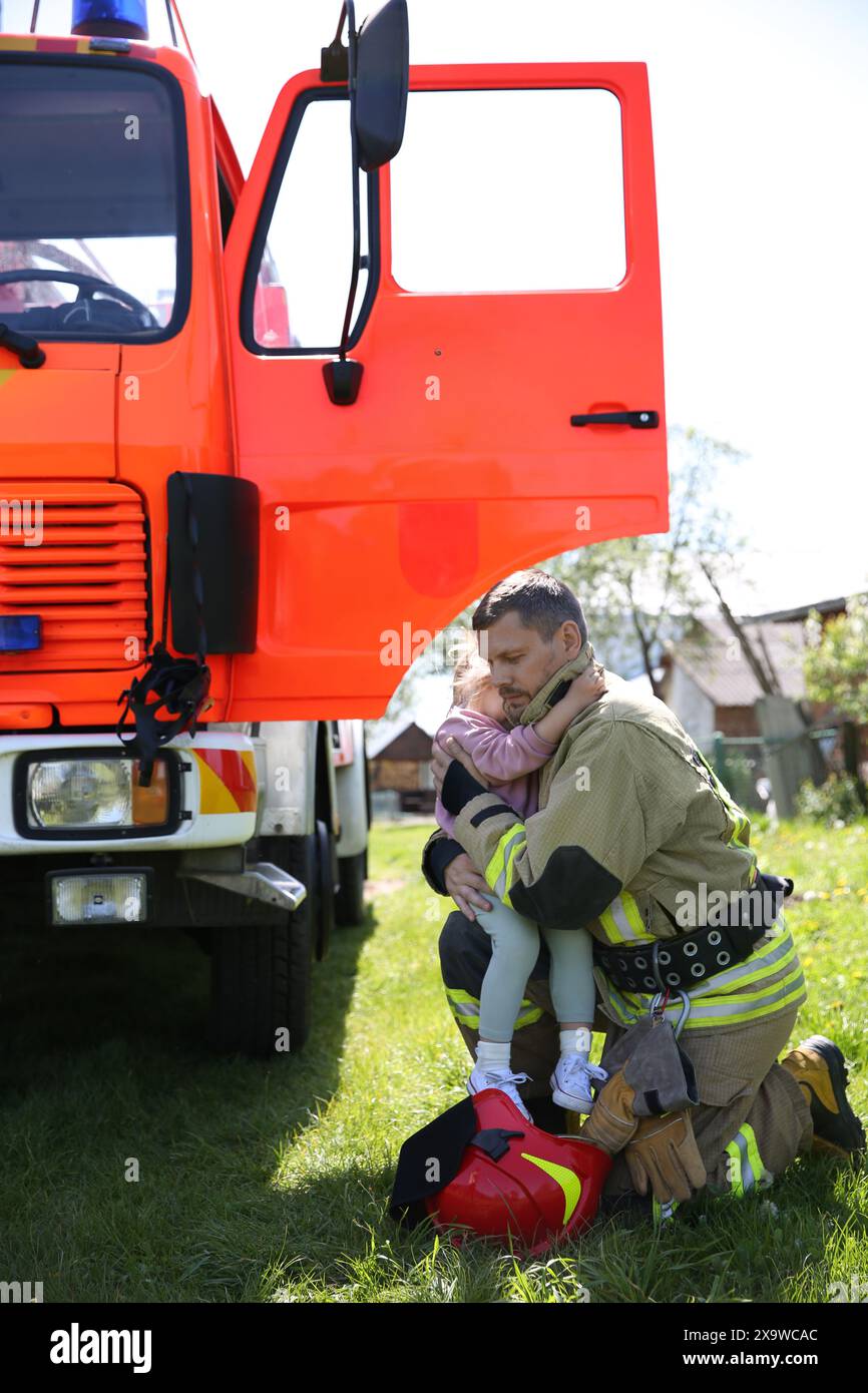 Firefighter in uniform with rescued little girl near fire truck ...