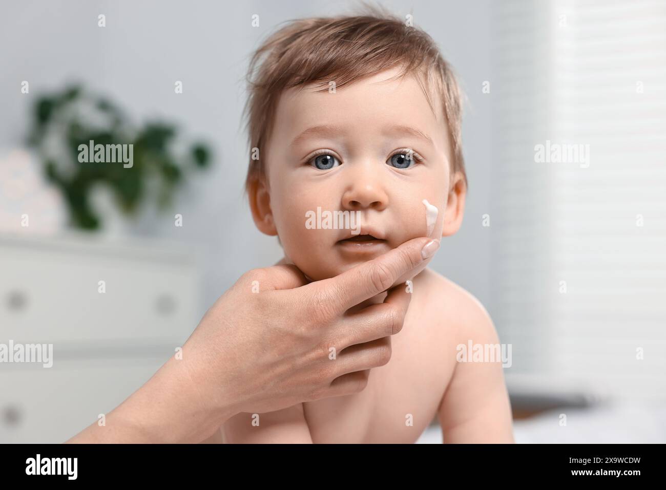 Mother applying moisturizing cream onto baby`s face indoors Stock Photo ...