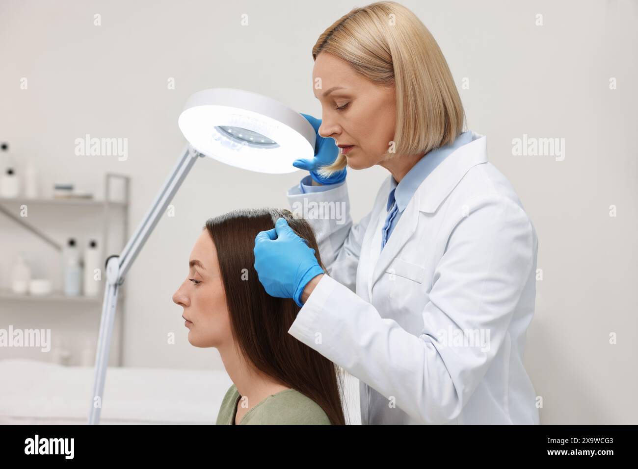 Trichologist examining patient`s hair under lamp in clinic Stock Photo ...