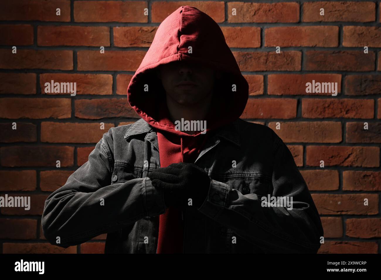 Thief in hoodie against red brick wall Stock Photo - Alamy