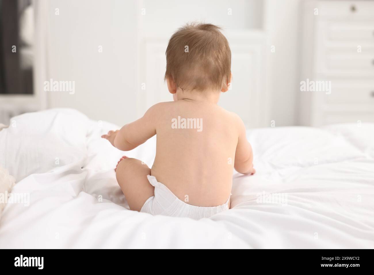 Baby boy sitting on bed at home, back view Stock Photo - Alamy